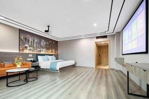 Quarto de hotel moderno com cama, sofá, escrivaninha e uma tela grande.