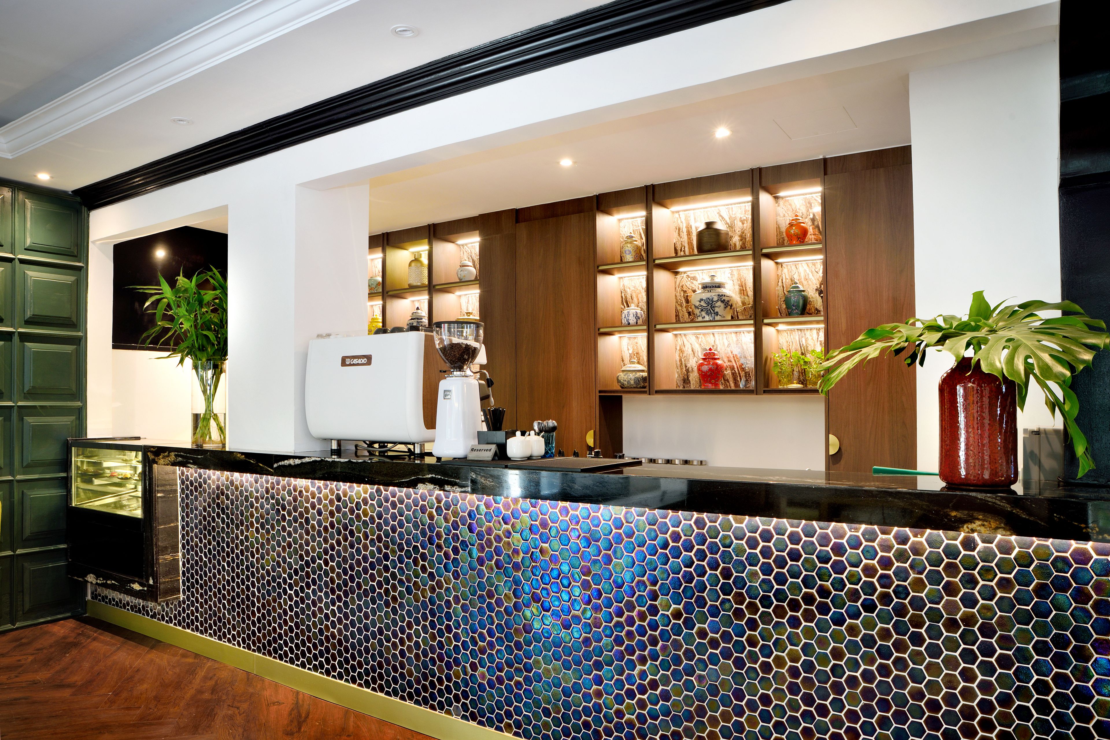 Cozinha moderna com bancada preta, máquina de café e exposição de objetos decorativos.