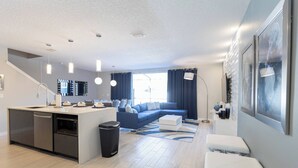 Uma cozinha moderna com uma ilha central, uma sala de jantar com sofá azul e uma sala de estar com uma grande janela.