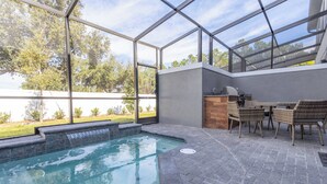 Piscina com estrutura de vidro, área de churrasco e assentos externos.