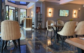 Um saguão de hotel moderno, com divisória de vidro, balcão de recepção e área de refeições com cadeiras e mesa.
