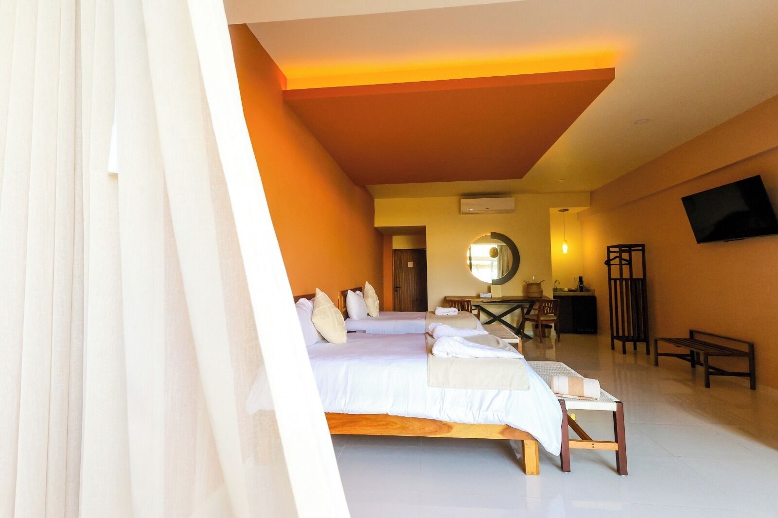 Quarto de hotel com três camas, uma escrivaninha, uma cadeira, uma televisão e um espelho.