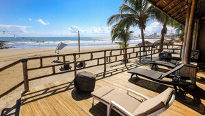 Um deck de madeira com espreguiçadeiras e uma estrutura de telhado de palha com vista para uma praia.