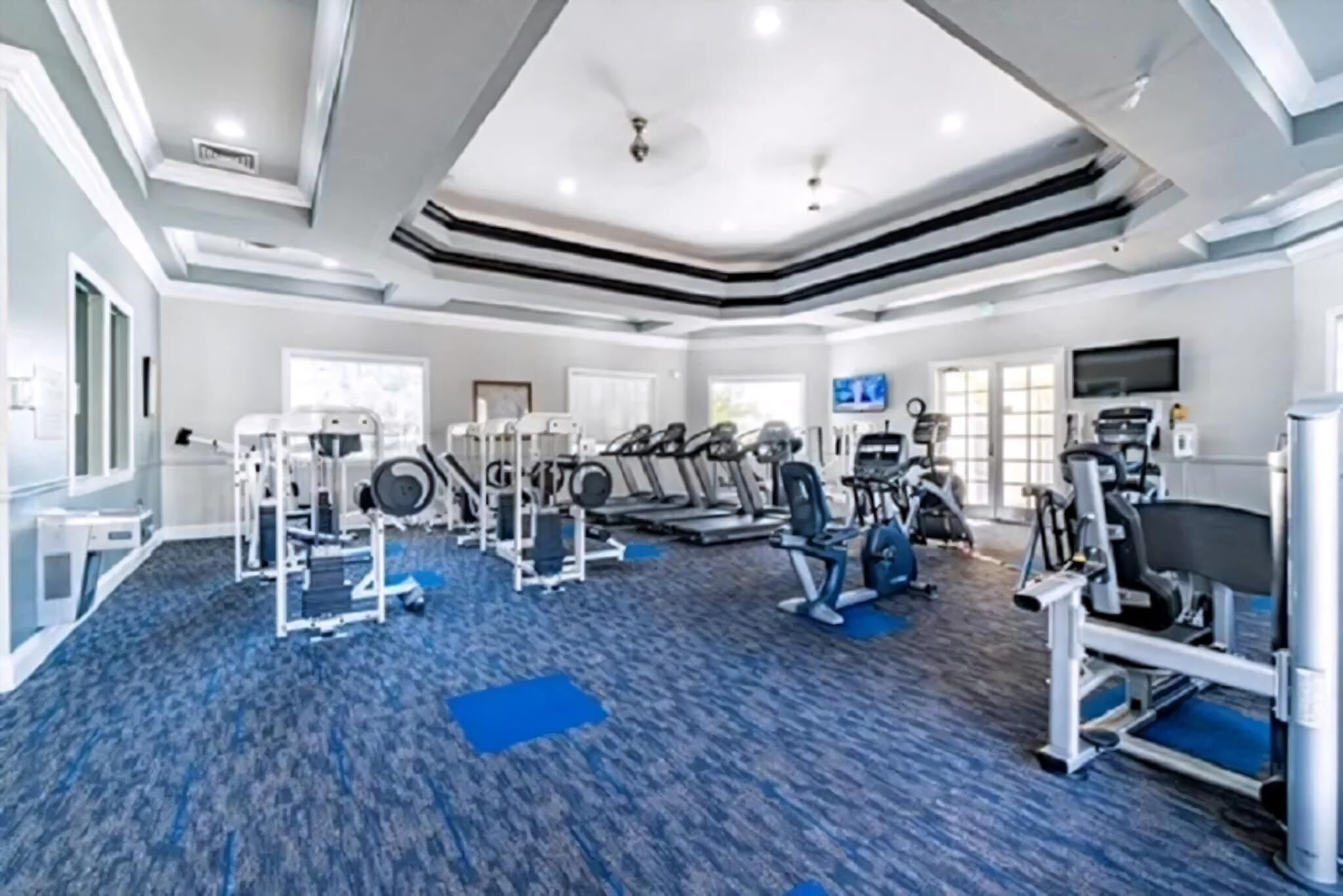 Uma academia espaçosa com diversos equipamentos de exercício, janelas amplas e um design moderno no teto.