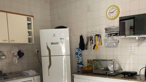 Uma cozinha com armários brancos, uma geladeira branca, micro-ondas e um relógio na parede.