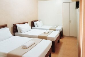 Quarto de hotel com três camas de solteiro, cada uma com roupa de cama e almofadas brancas, e um guarda-roupa com duas portas.