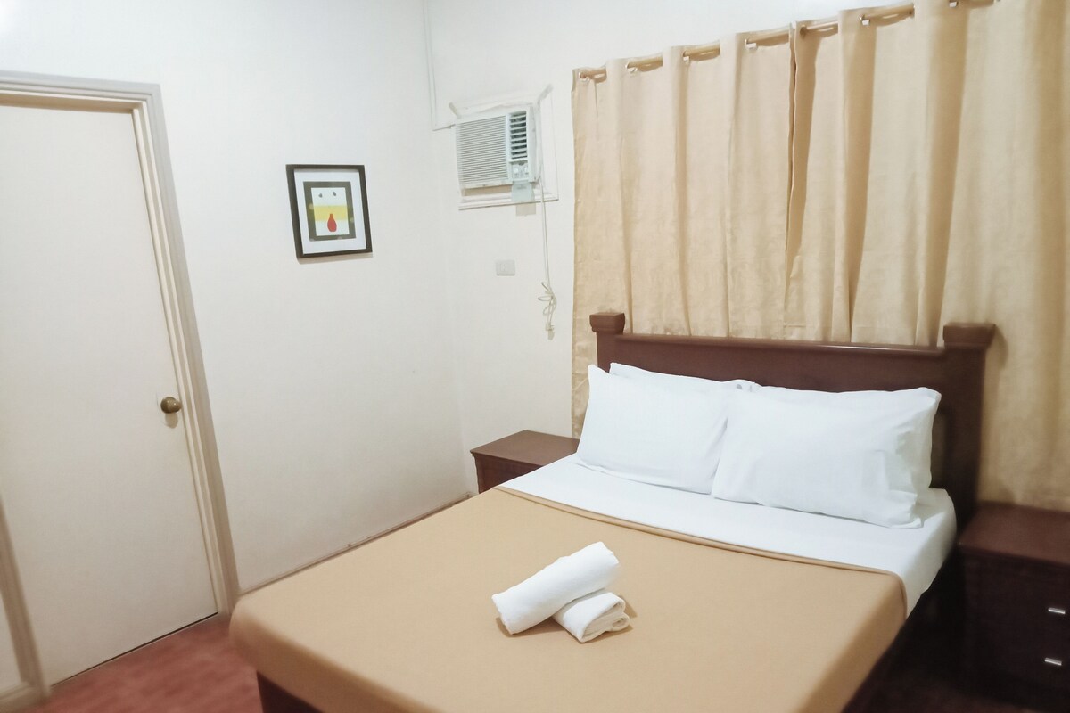 Quarto de hotel com cama, mesa de cabeceira, porta e janela com cortinas.