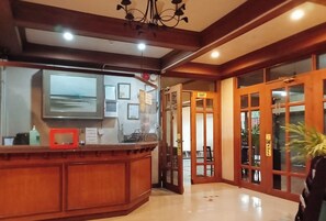 Uma área de recepção com balcão de madeira, televisão montada e certificados emoldurados na parede.