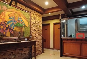Quarto com parede de pedra, balcão de madeira e um espelho grande. Há uma porta que dá para outro quarto.