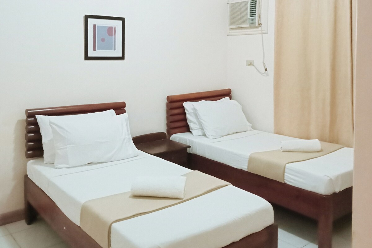 Duas camas de solteiro com cabeceiras de madeira, roupa de cama branca e uma pequena moldura na parede.
