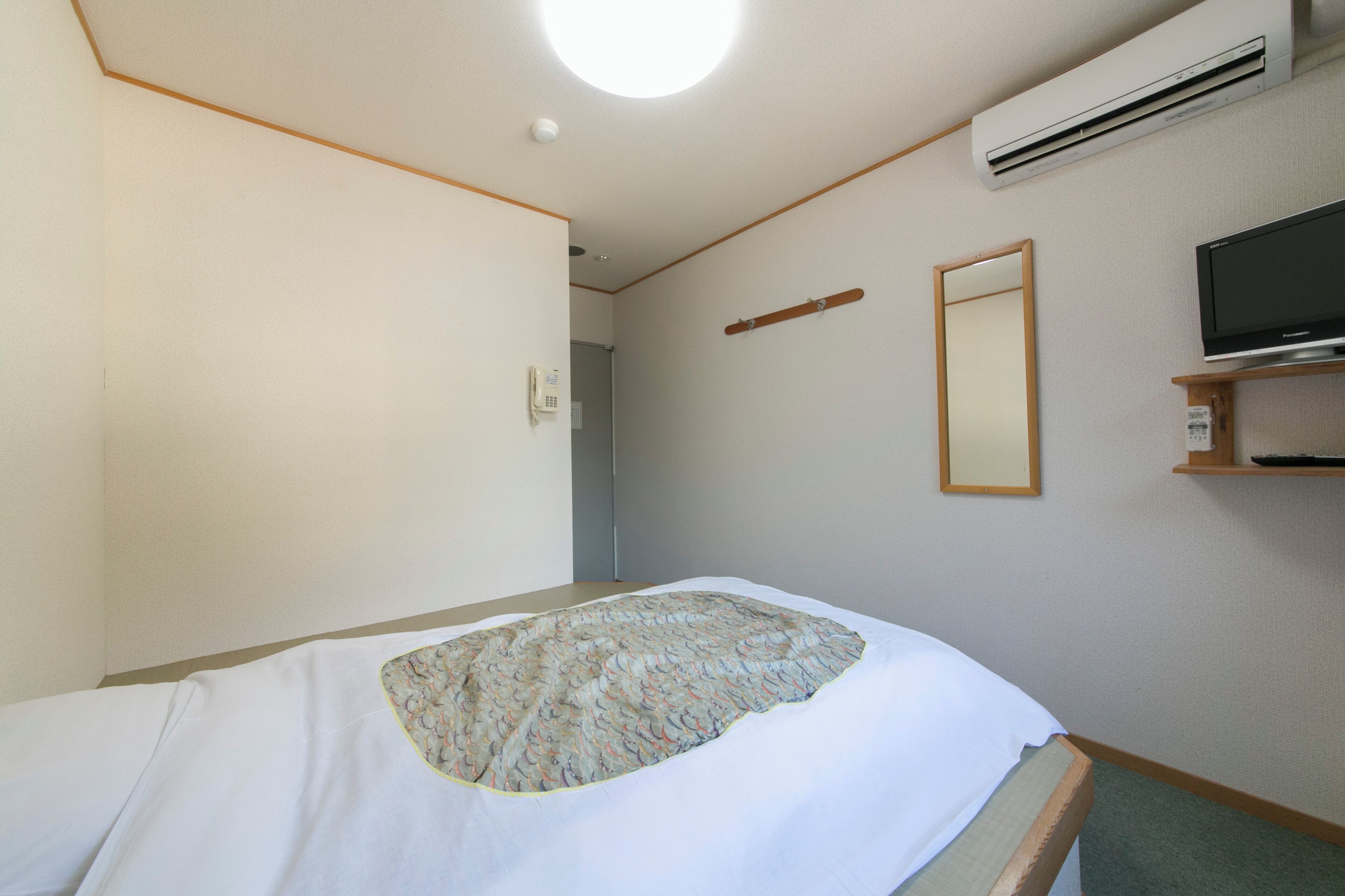 Quarto de hotel com cama, ar condicionado, televisão e espelho.