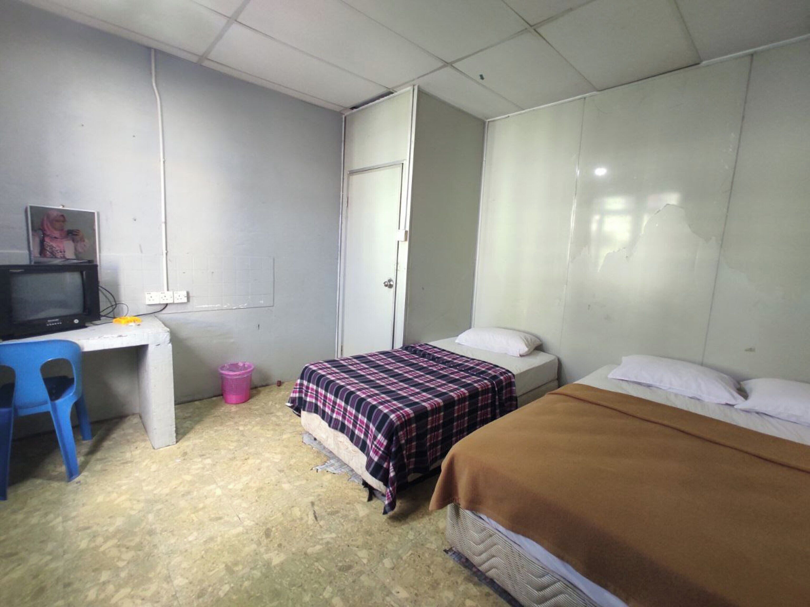 Quarto pequeno e compacto com uma cama de solteiro, uma escrivaninha com televisão e um guarda-roupa.