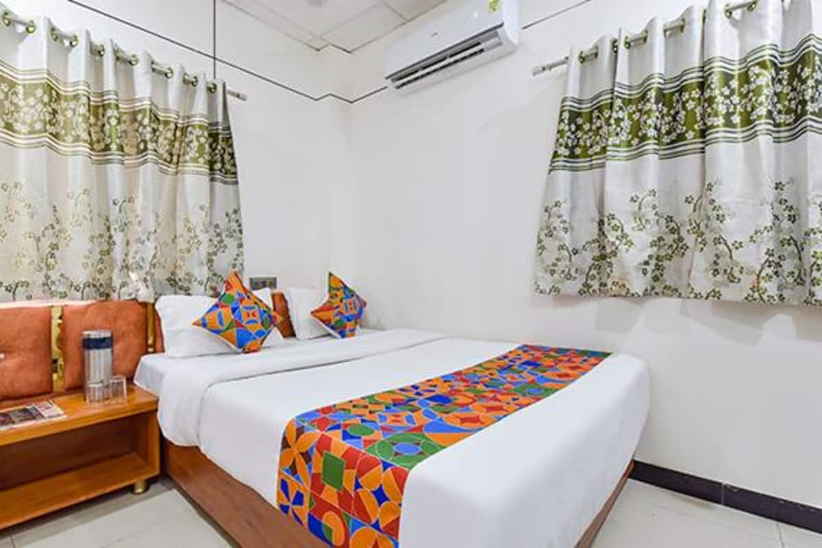 Quarto de hotel com uma cama, uma mesa de cabeceira de madeira, um edredom colorido e cortinas florais.