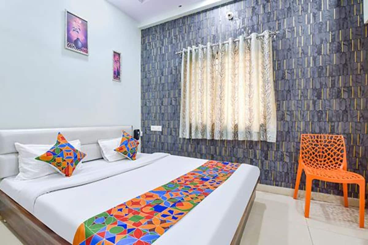 Quarto com cama, almofadas, manta colorida, cadeira e papel de parede estampado.