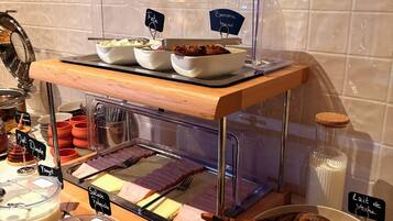 Buffet com diversas opções de comida, incluindo uma saladeira de frutas, um pote de iogurte e seleção de queijos.
