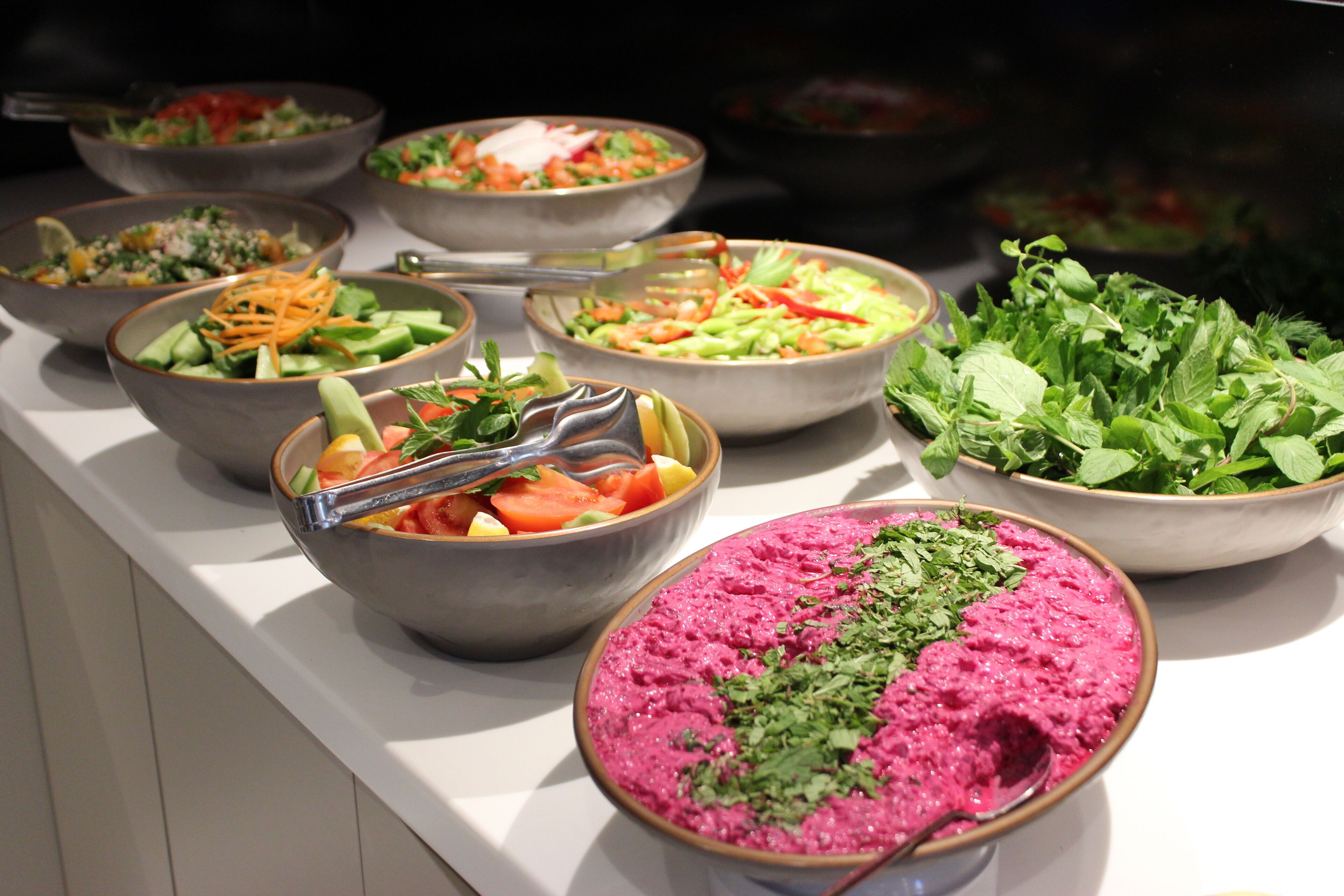 Uma mesa de buffet com diversos pratos, incluindo saladas, um patê de beterraba e uma saladeira.