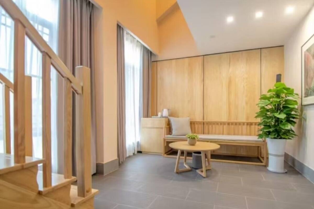 Um hall de hotel moderno com um banco de madeira, uma mesa redonda com uma planta e uma escadaria com corrimãos de madeira.
