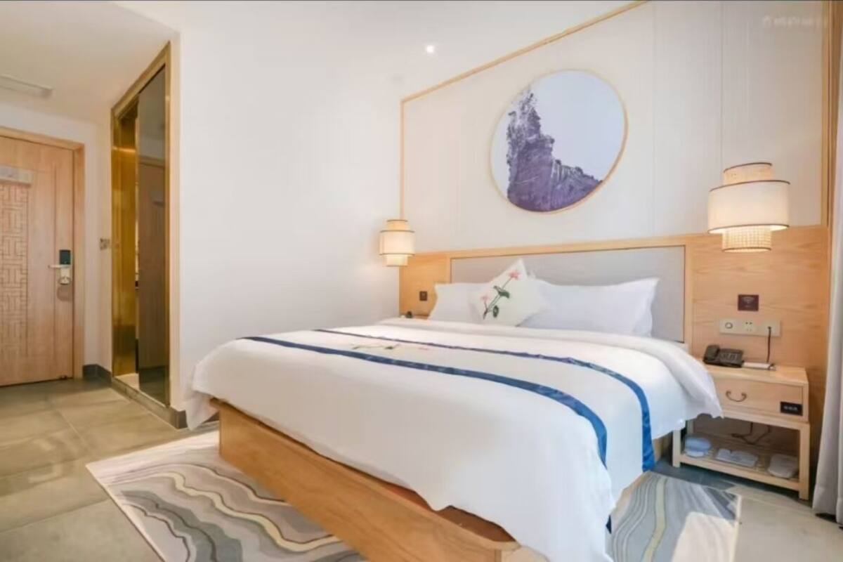 Quarto de hotel com cama de madeira, uma grande imagem pendurada na parede, duas luminárias de cabeceira e mesa de cabeceira com telefone.