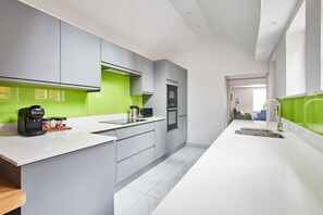 Uma cozinha moderna com armários cinzas, bancada branca e painel de fundo verde, além de forno embutido.