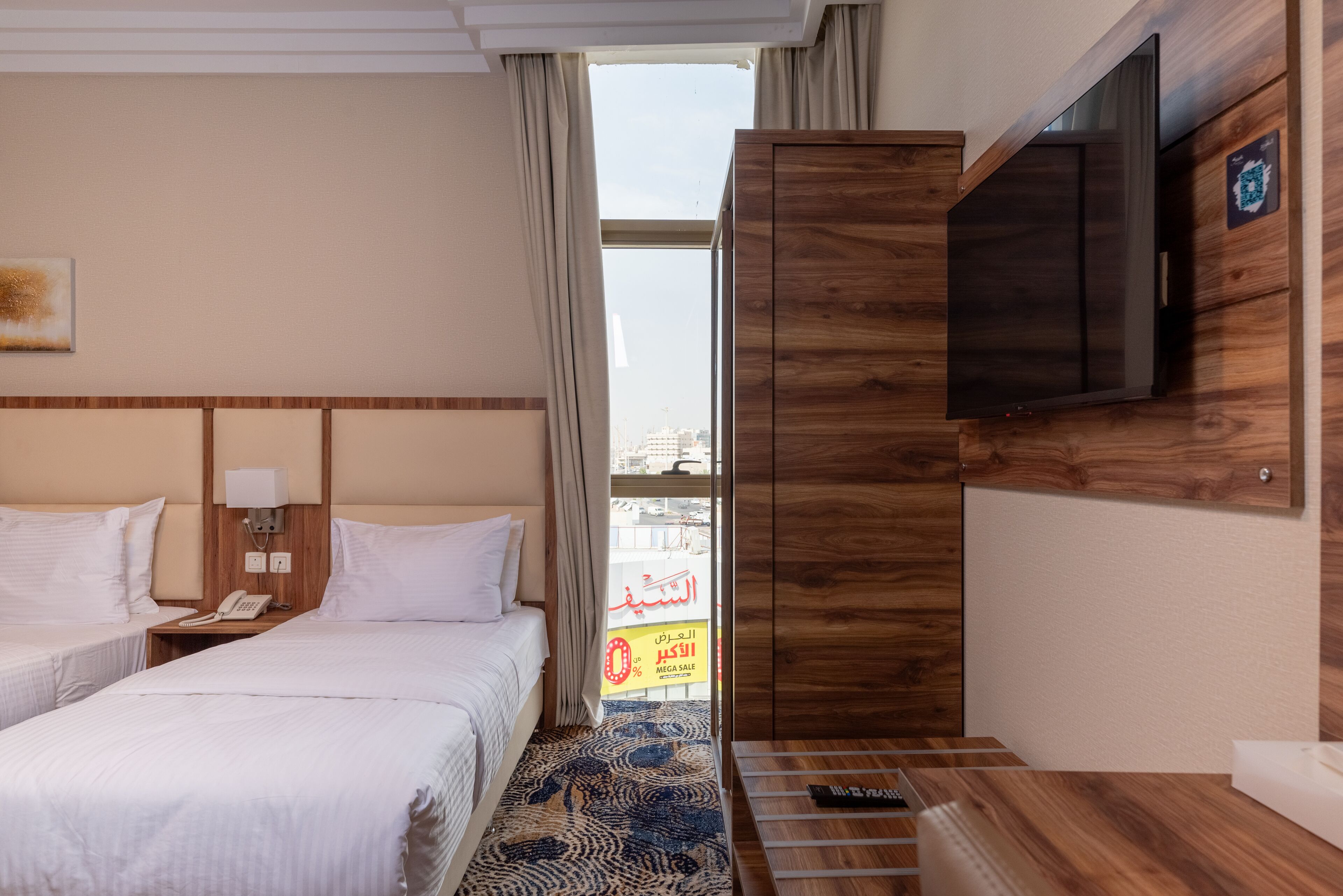 Quarto de hotel com duas camas, um guarda-roupa de madeira, televisão, telefone e tapete estampado.
