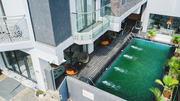 Uma área de piscina no terraço com guarda-corpos de vidro, espreguiçadeiras e plantas em vasos.