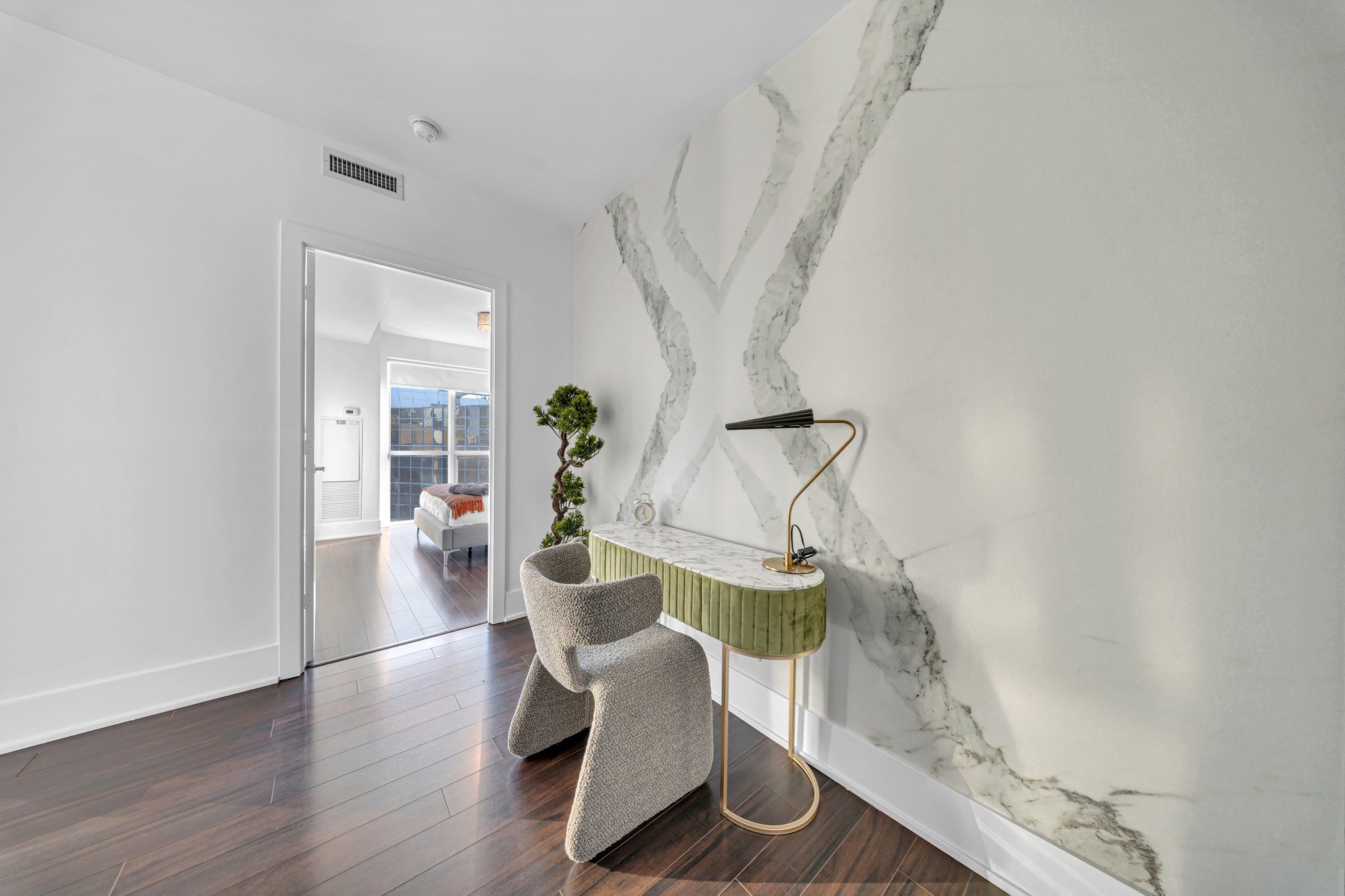 Um interior moderno com parede de mármore, soalho de madeira, uma cadeira singular e uma pequena mesa com uma luminária.