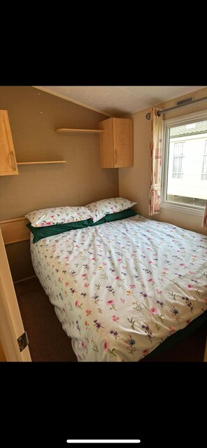 Cama com colcha estampada em flor e travesseiros verdes em quarto com armários de madeira e janela com cortinas.