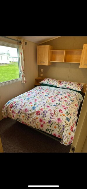 Quarto com colcha florida, cabeceira de madeira e janela com cortinas.