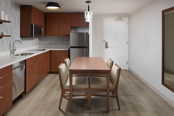 Uma cozinha moderna com armários de madeira, eletrodomésticos de aço inoxidável, uma mesa de jantar com cadeiras e uma luminária pendente.