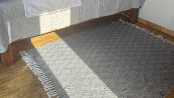 Uma cama de solteiro com colcha acolchoada e almofadas, um tapete estampado e um sonho apanhador pendurado no teto.