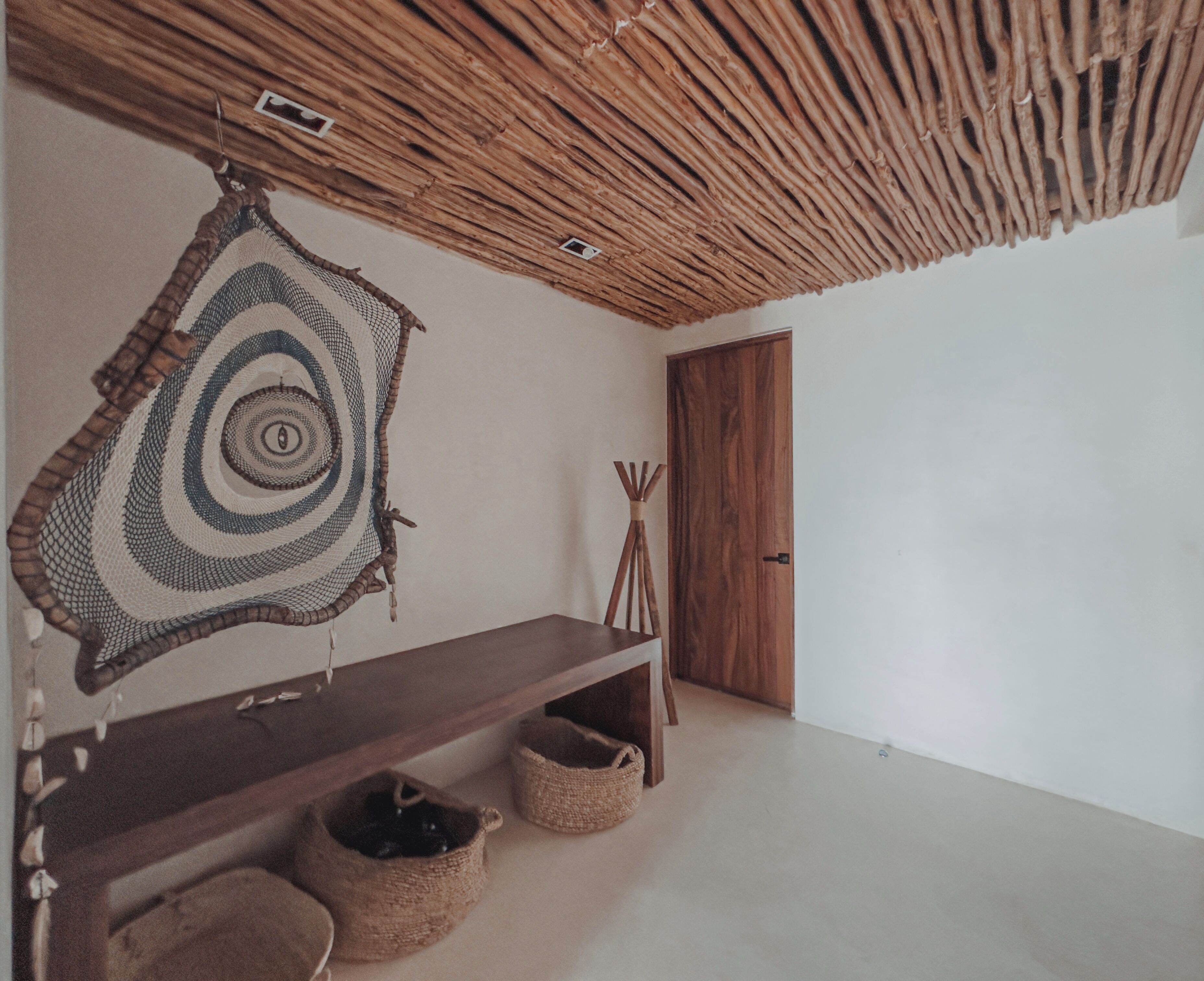 Quarto com tapeçaria na parede, porta de madeira, prateleira com cestos e tapete de fibra natural no chão.