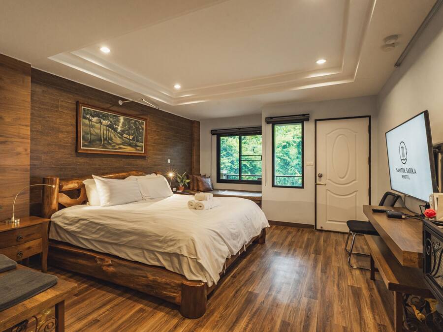 Quarto com cama de madeira, escrivaninha, computador e janela com vista para o verde.