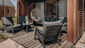 Uma cabana de madeira com varanda, com área de estar externa, incluindo uma cadeira suspensa e dois sofás.