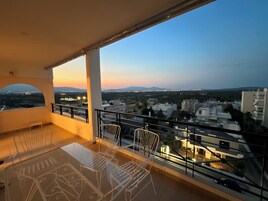 Uma varanda com mesa e cadeiras de vidro, com vista para o horizonte urbano ao entardecer.
