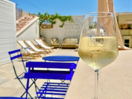 Um copo de vinho branco sobre uma mesa com cadeiras e toalha de mesa azuis.
