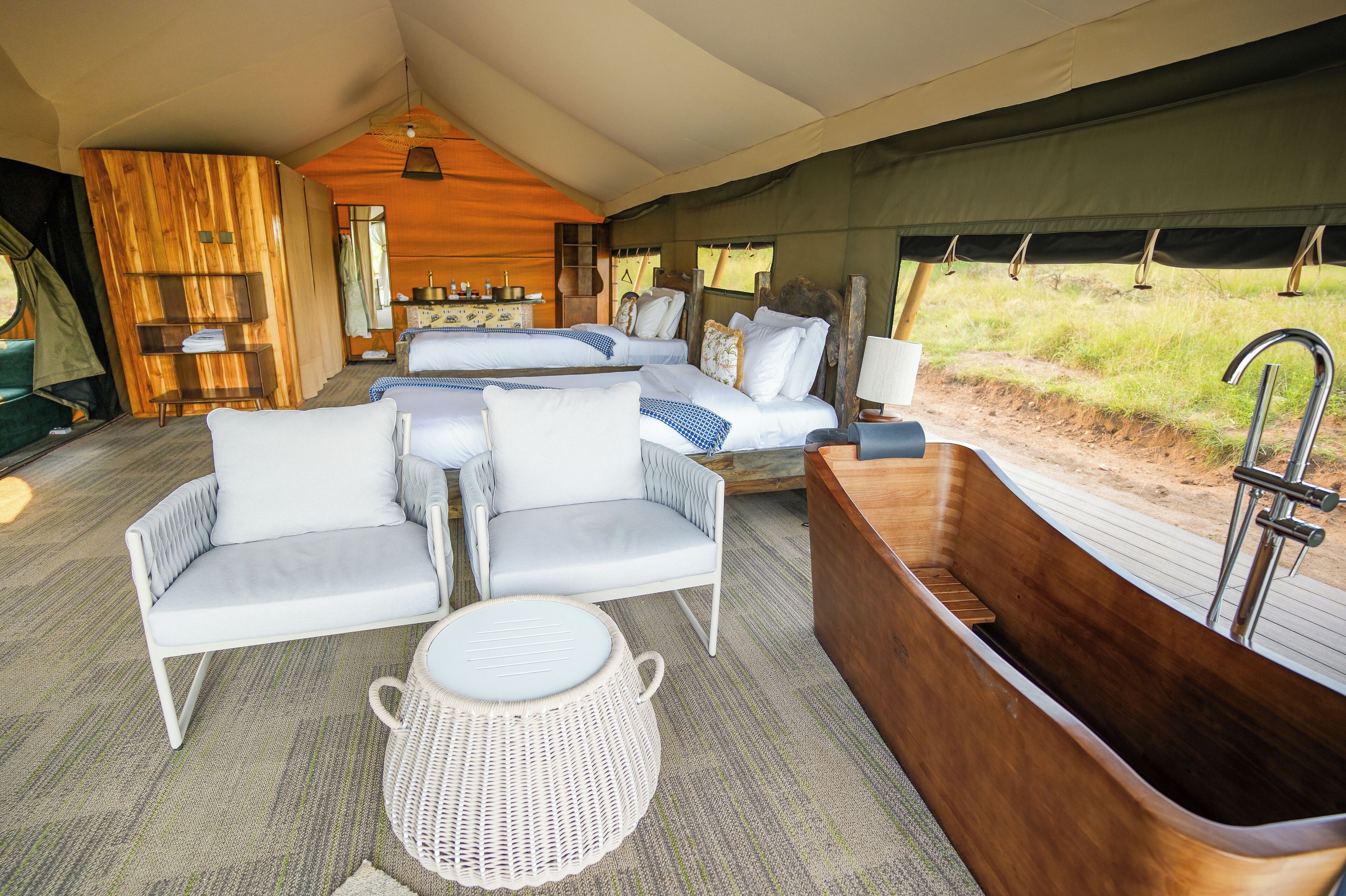 Acomodação em tenda com duas camas, uma banheira de madeira, um sofá e uma pequena mesa redonda.