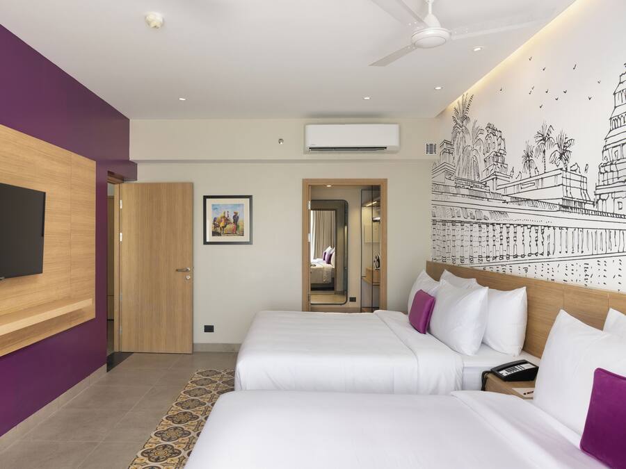 Quarto de hotel com duas camas, uma TV de tela plana, um mural grande e um ventilador de teto.