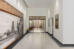 Corredor moderno de hotel com um mural grande, área de recepção e espaço de estar com vista para o interior.