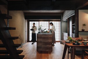 Um interior moderno com uma mesa de jantar de madeira, uma ilha central com uma pia e uma vista através de grandes biombos shoji.