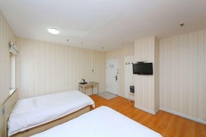 Quarto com duas camas, uma mesinha, televisão e porta.