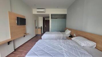 Quarto de hotel com duas camas, televisão fixada na parede, cabeceira de madeira e uma pequena mesa de trabalho com um espelho.