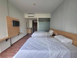 Quarto de hotel com duas camas, televisão fixada na parede, cabeceira de madeira e uma pequena mesa de trabalho com um espelho.