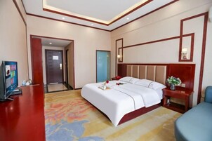 Quarto de hotel com cama, mesa de cabeceira e escrivaninha com computador.