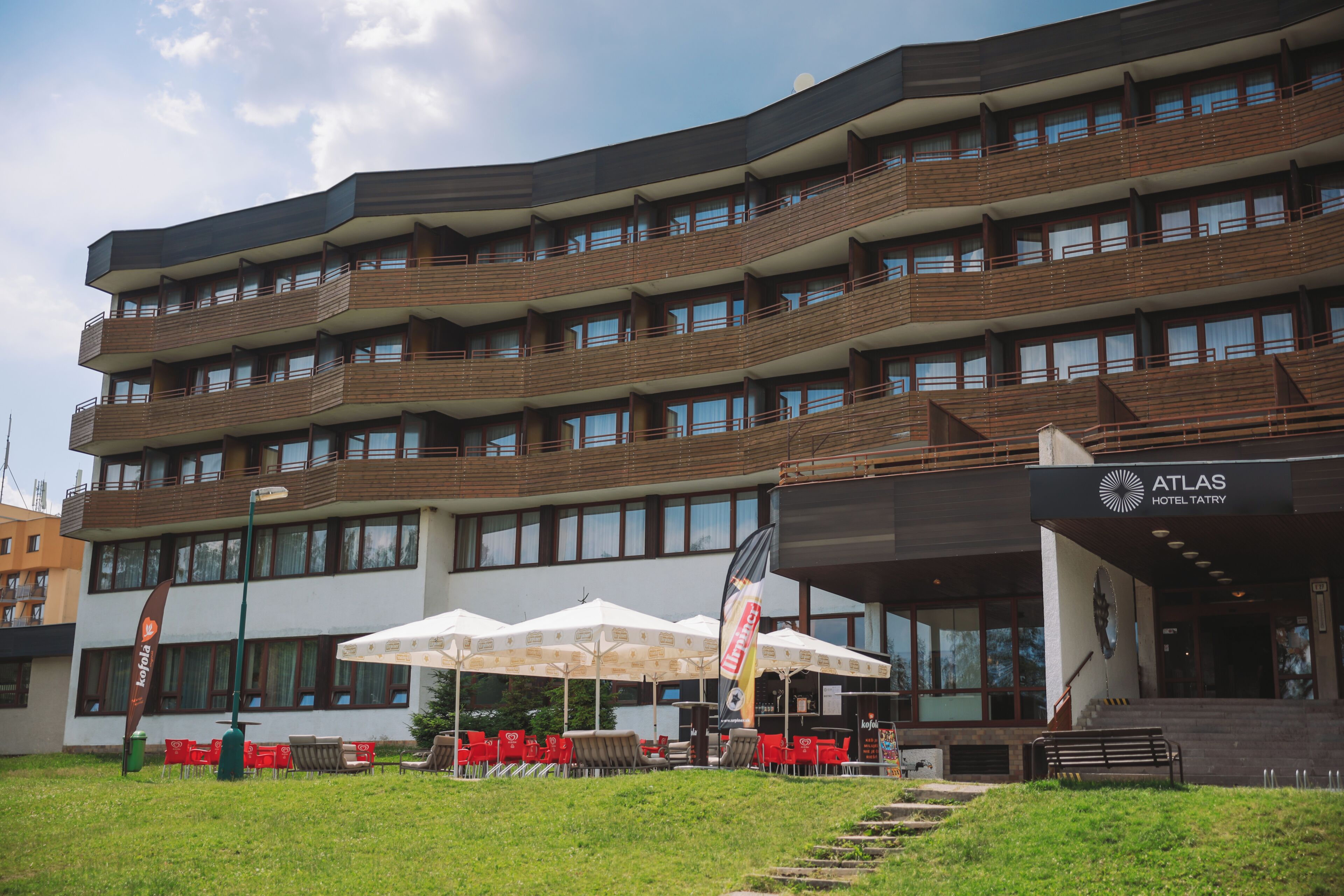 Um hotel com vários andares, mesas ao ar livre e uma placa com a inscrição 'Atlas Hotel Tatry'.