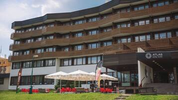 Um hotel com vários andares, mesas ao ar livre e uma placa com a inscrição 'Atlas Hotel Tatry'.