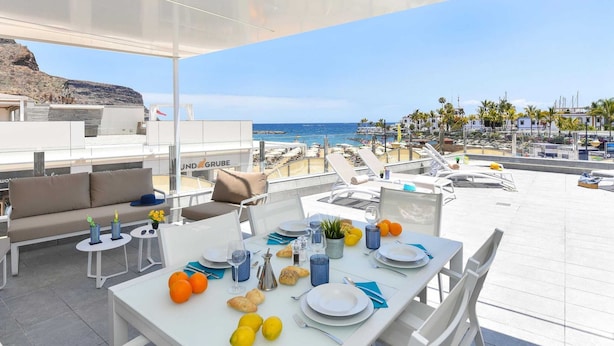 Uma área de refeições no terraço com uma mesa posta para dois, com vista para a praia e o mar.