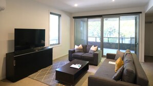 Uma sala de estar moderna com televisão de tela plana, um sofá, uma mesa de centro e uma porta de vidro deslizante que dá para uma varanda.
