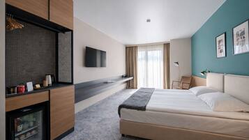 Quarto de hotel moderno com cama, televisão, frigobar e escrivaninha.