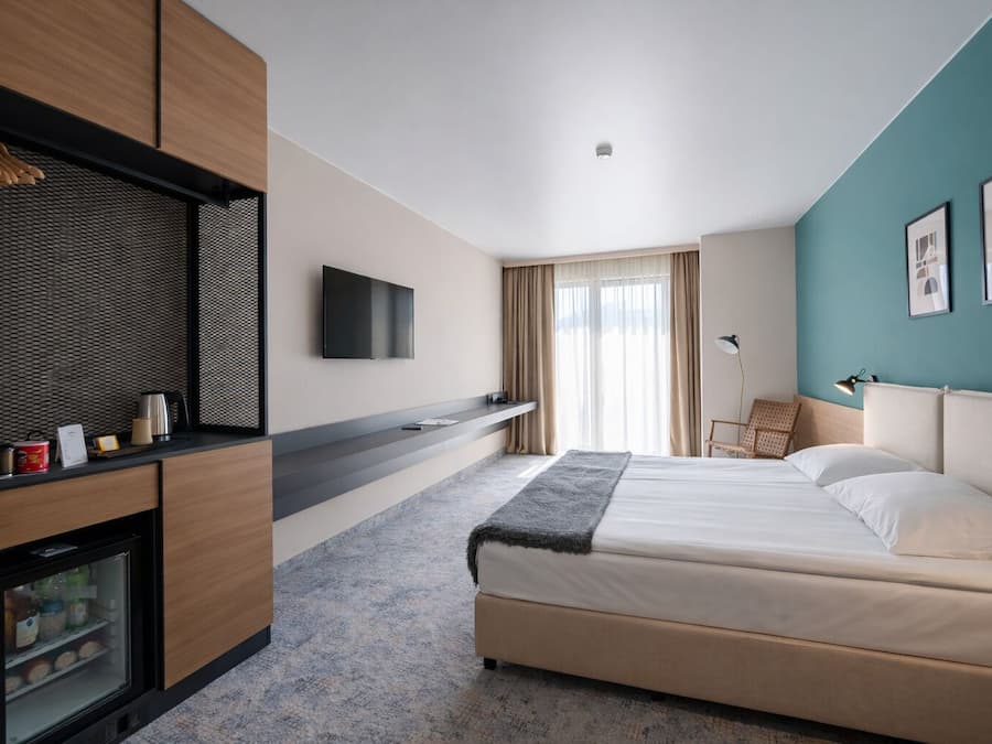 Quarto de hotel moderno com cama, televisão, frigobar e escrivaninha.
