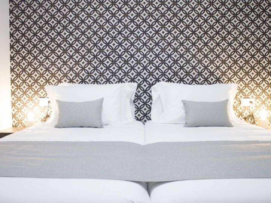 Cama bem arrumada com lençóis brancos e duas almofadas, em frente a um papel de parede estampado.